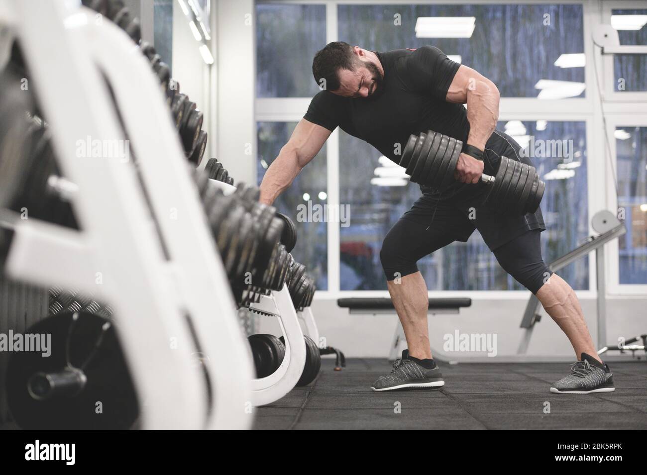 strong young bearded man in black sportswear pulling heavy weight ...