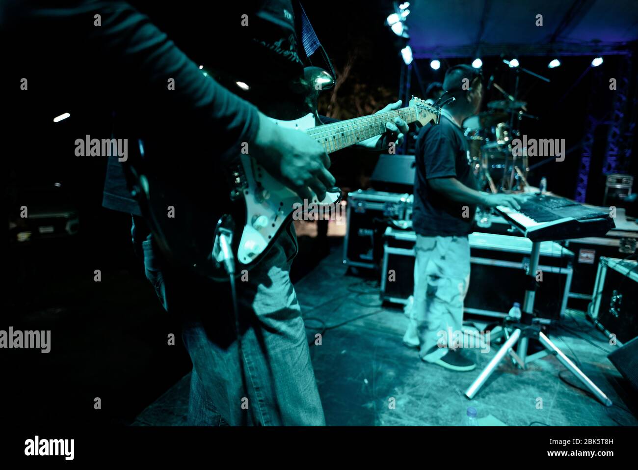 Rock band performs live at rock show on stage. Guitarist, bass guitar ...