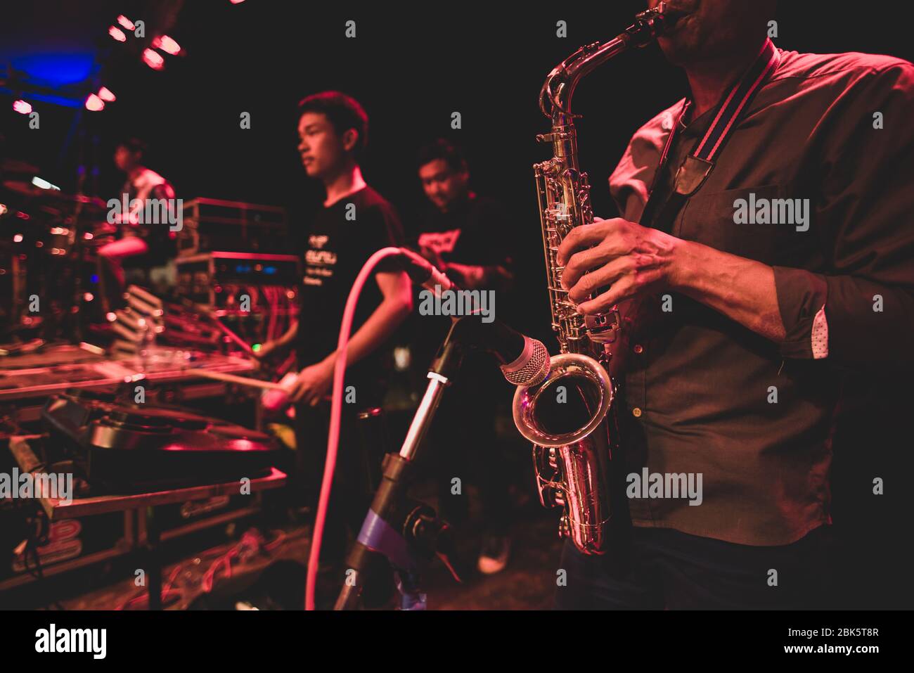 Rock band performs live at rock show on stage. Guitarist, bass guitar ...