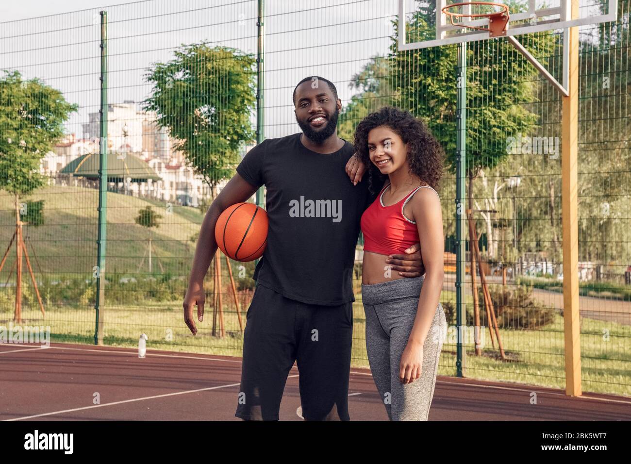 Outdoors Activity. African couple standing with ball hugging on ...