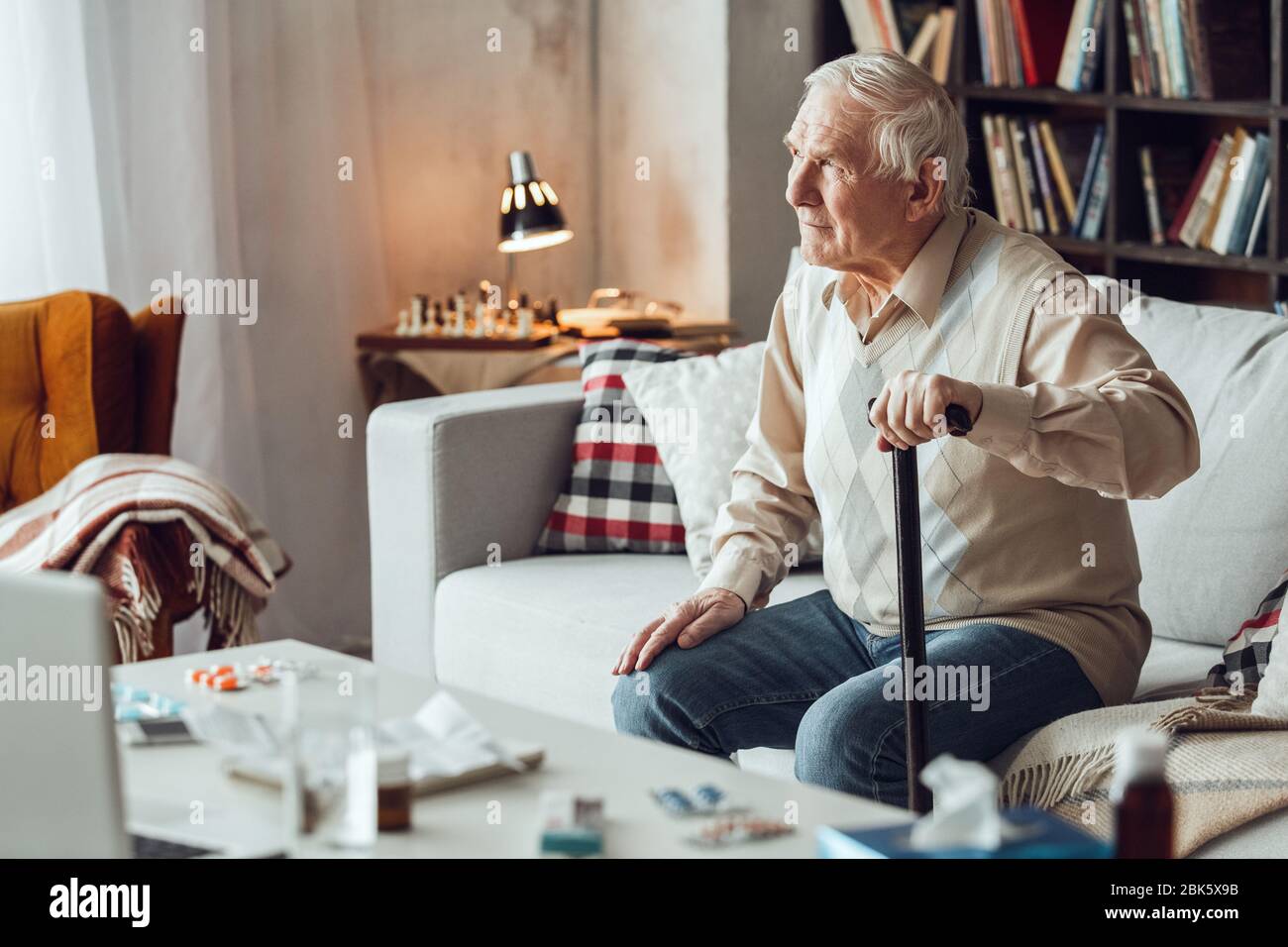 Senior man alone sitting at library with walking stick looking out the ...