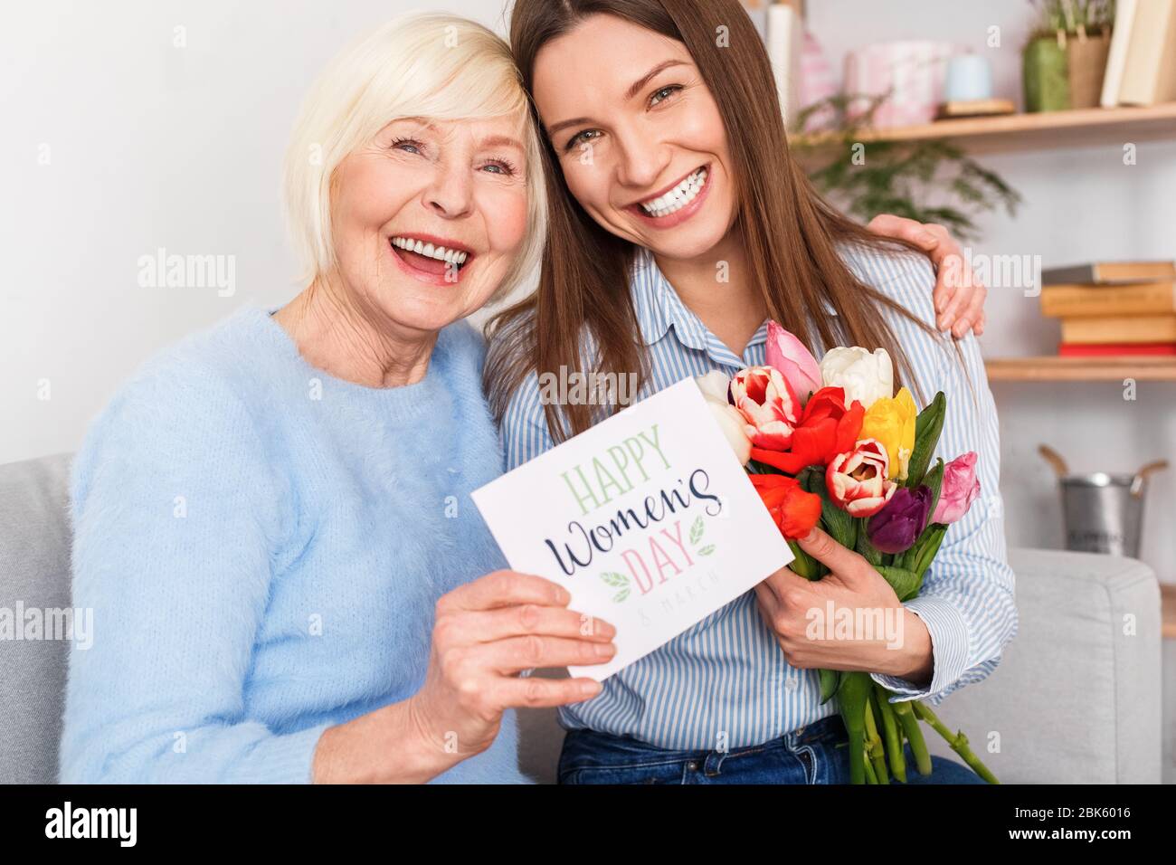 Adult daughter and her retirement mother holding postcard and tulips in ...