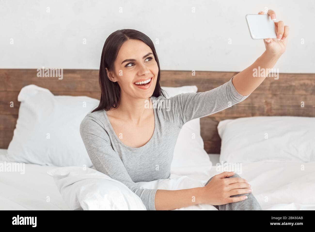Bedtime. Woman sitting on bed taking selfie on smartphone smiling playful Stock Photo - Alamy