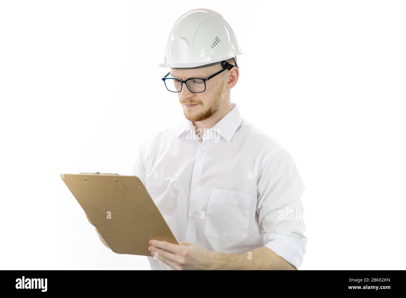 Handsome architector in hard hat makes notes on clipboard on white ...