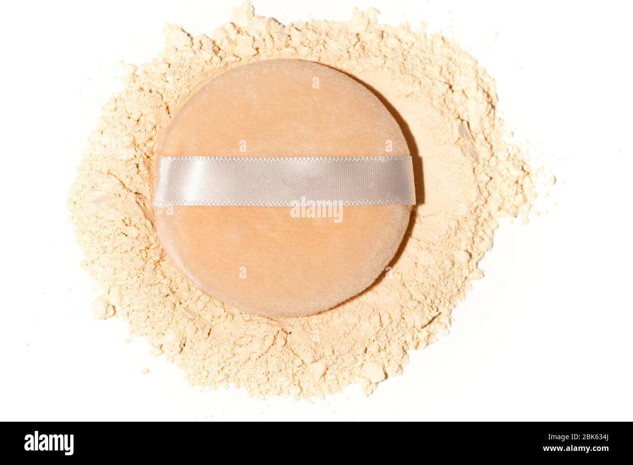 Scattered tan colored facial loose powder and puff on white background ...