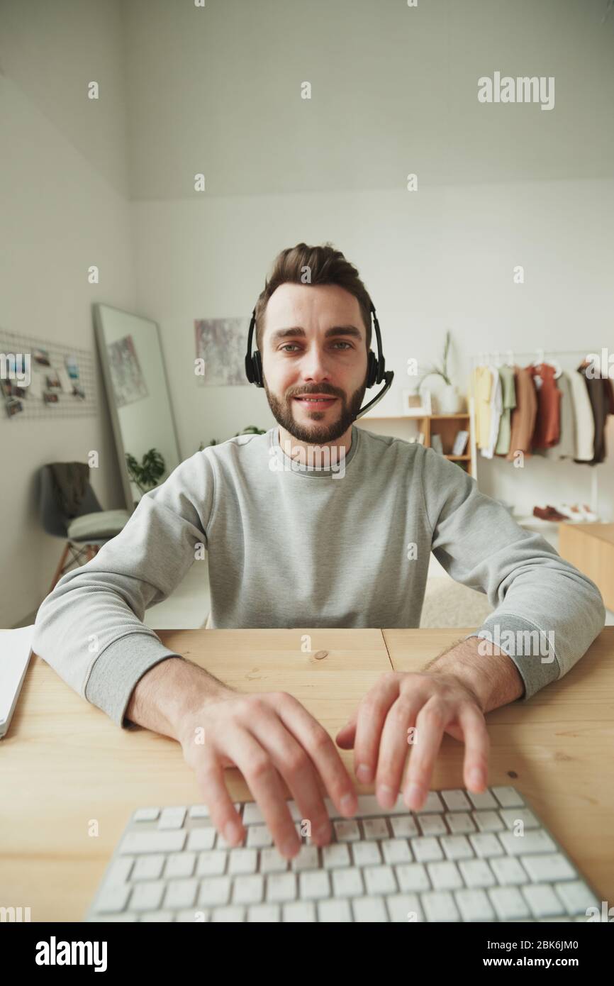 Young friendly operator with headset typing on computer keypad while ...