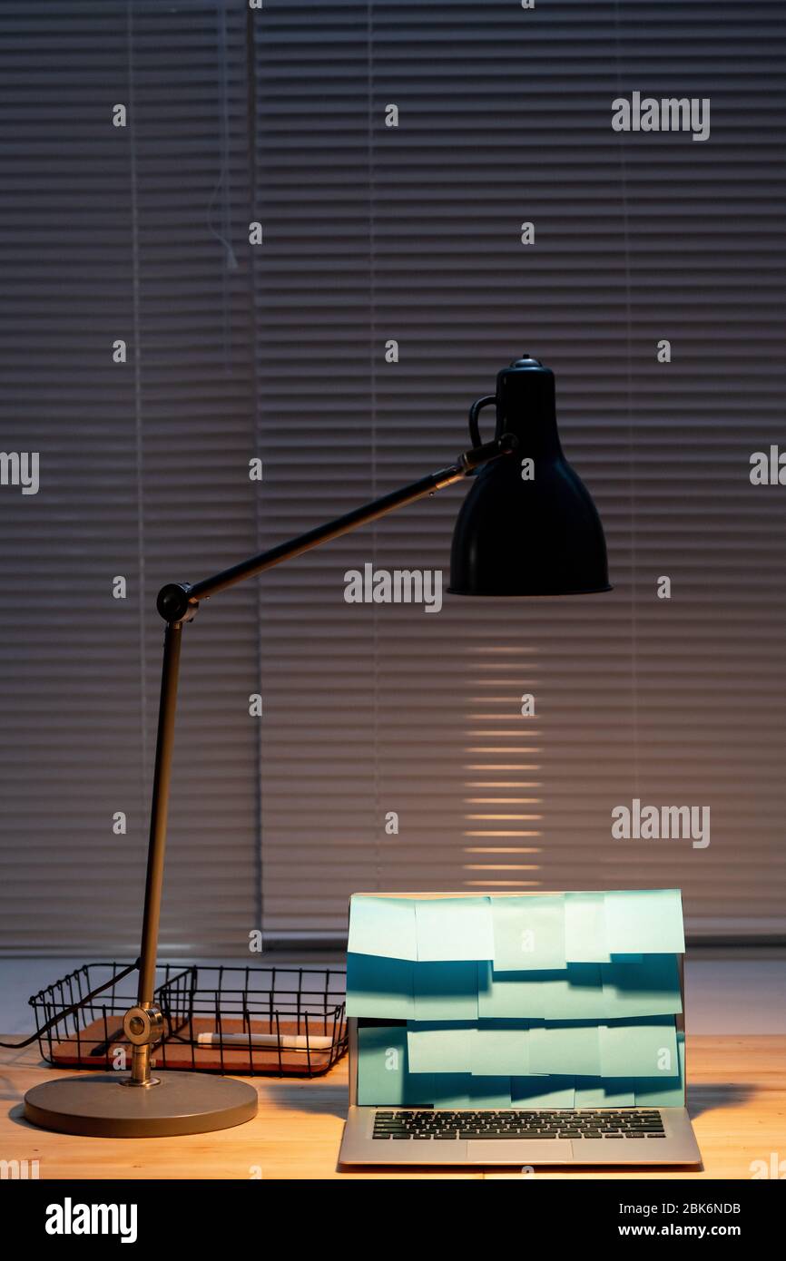 Light of lamp over laptop with blue notepapers on display and basket ...