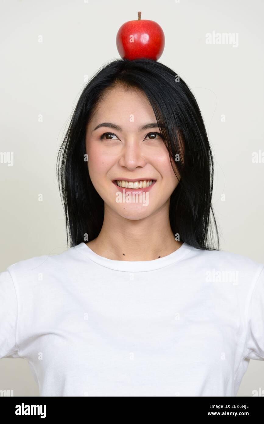 Happy young beautiful Asian woman thinking with apple on top of head ...