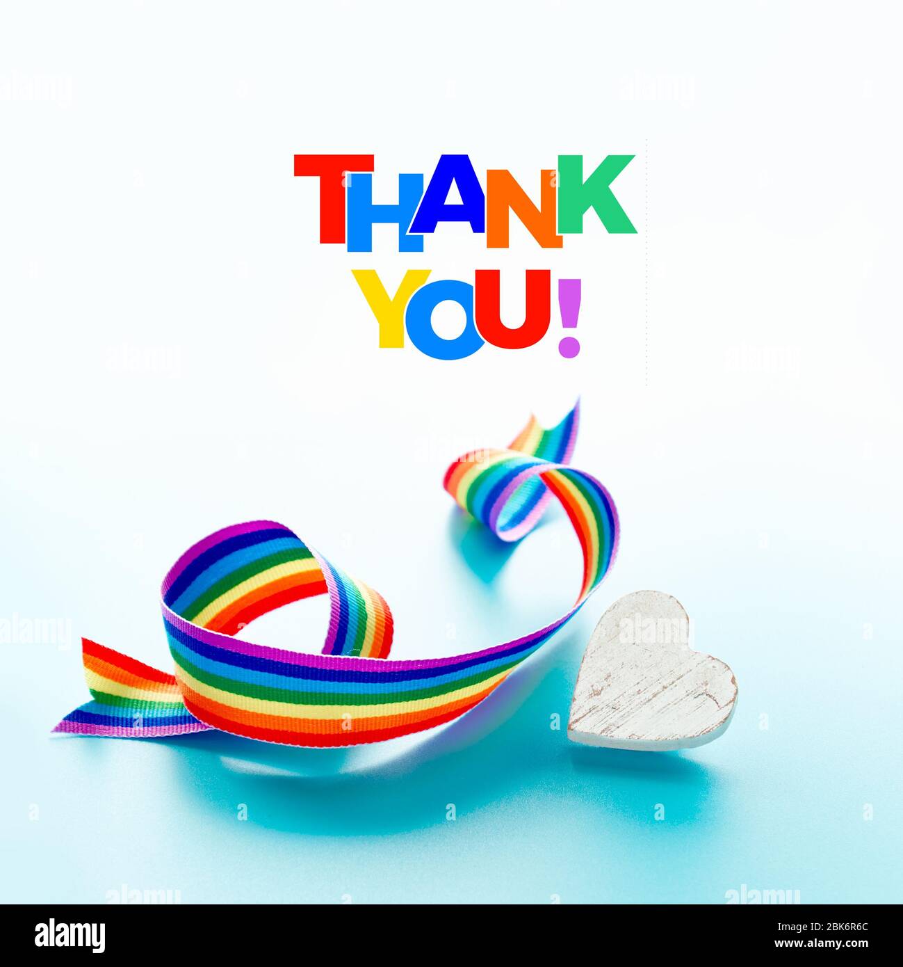 Wooden heart and curled rainbow ribbon. Rainbow text "Thank you" on ...