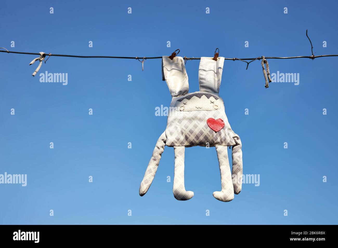 Forgotten old faded toy of bunny hanging on a clothesline on background ...