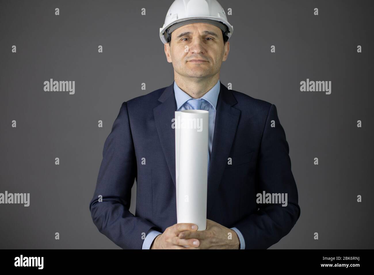 Handsome architect in hard hat holds blueprint roll confidently looks ...
