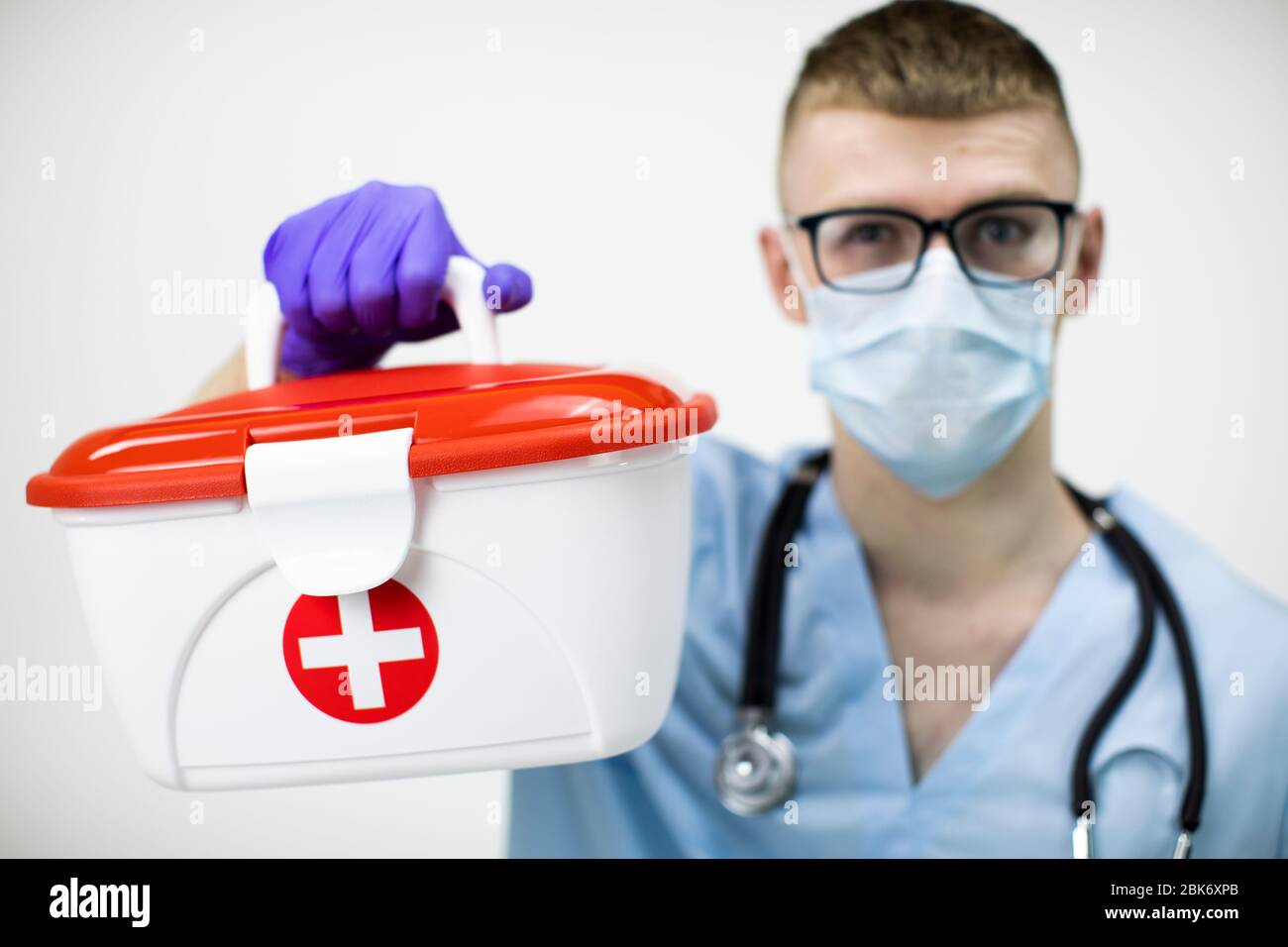 paramedic in mask, glasses and blue latex gloves holds red cross ...