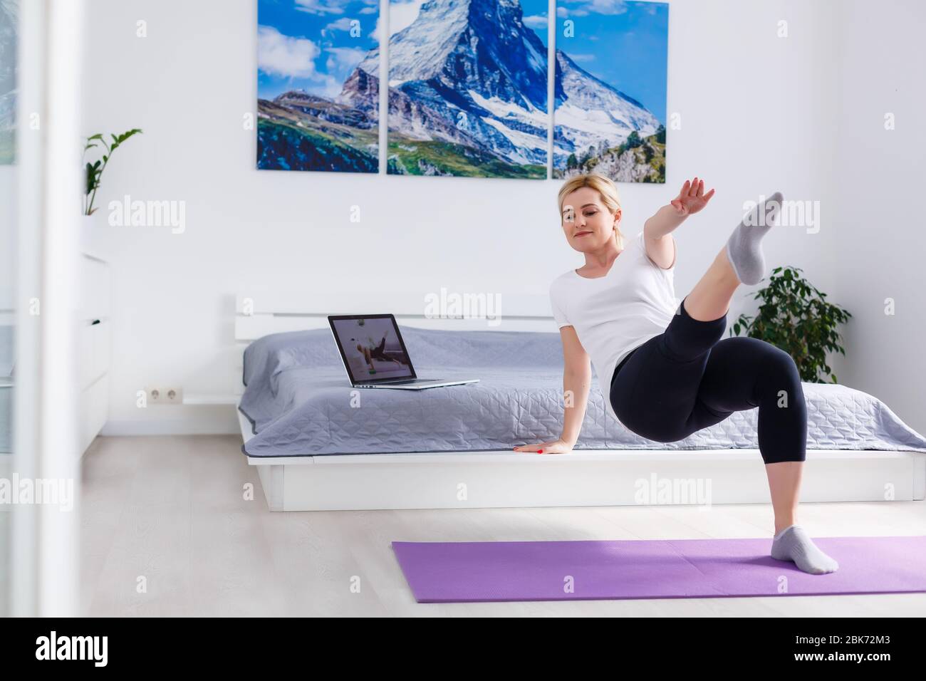 Happy woman doing exercise while watching workout video on laptop at ...