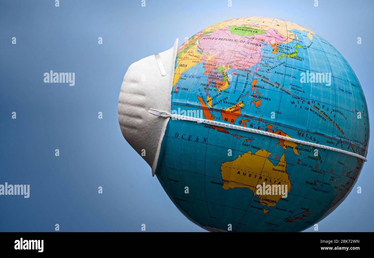 Face mask around a world globe in side view over a grey background with ...