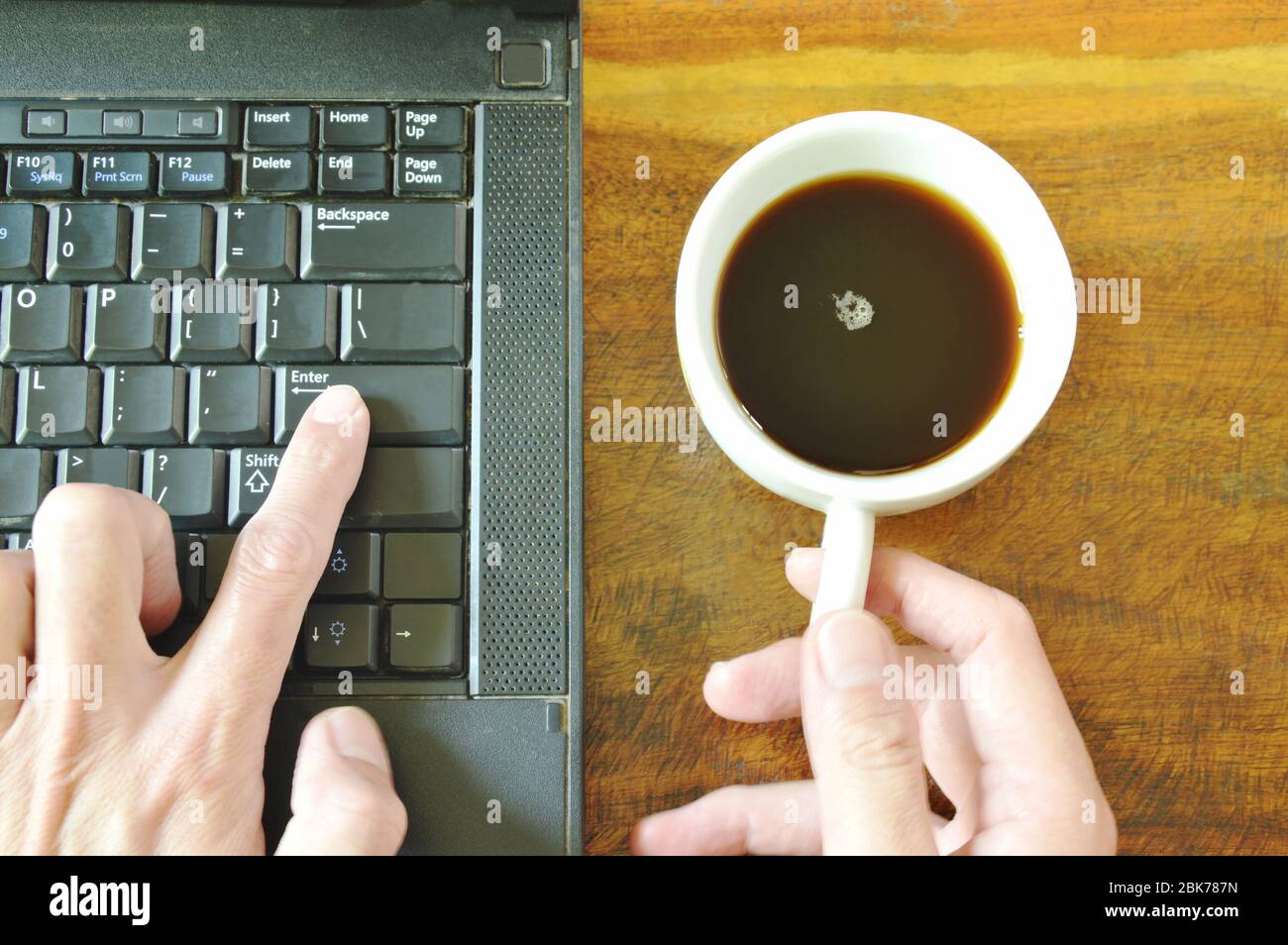 finger pushing enter button on computer notebook while holding coffee ...
