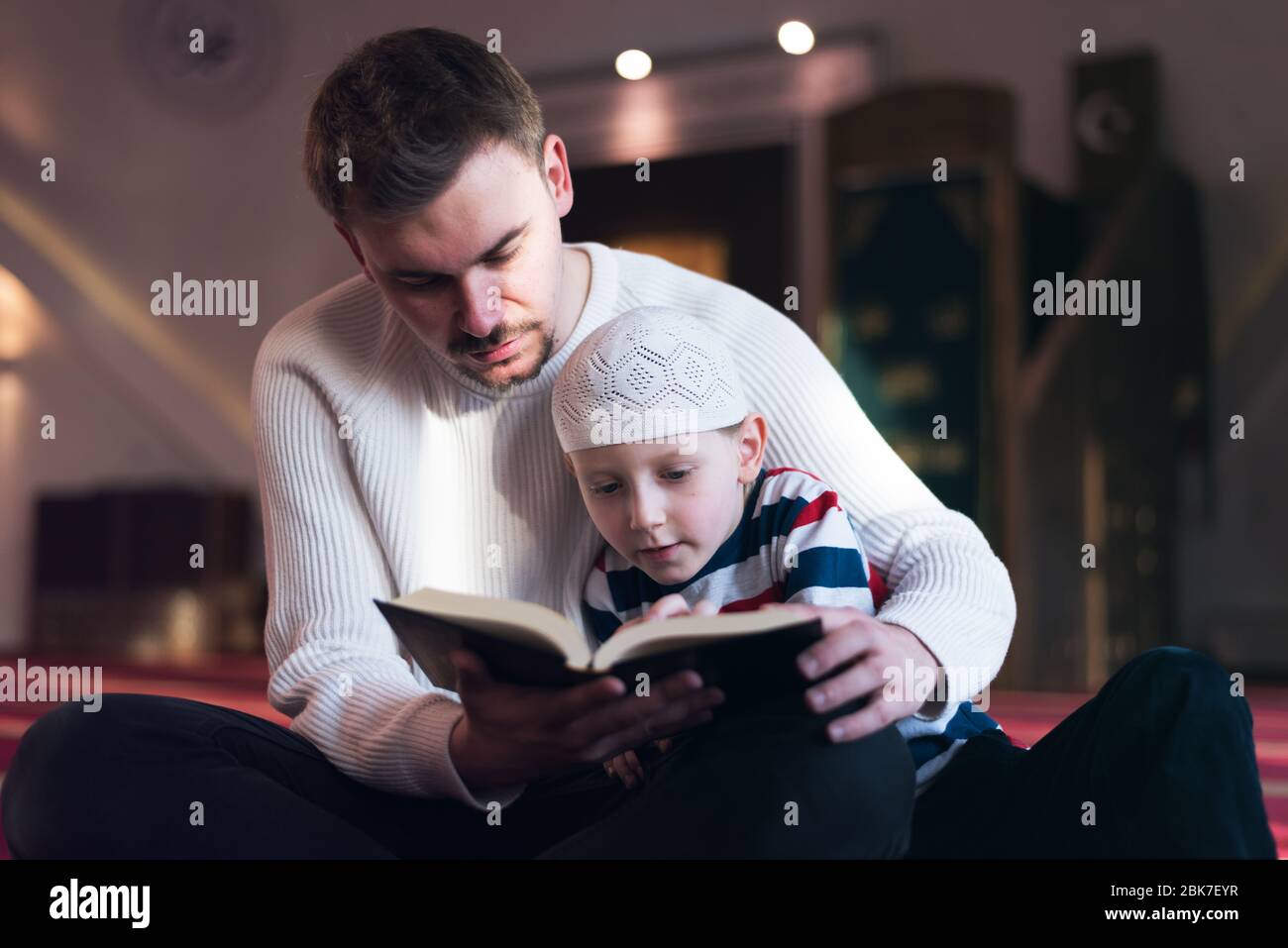 Religious Muslim Man teaching his little son to pray to God with Koran ...