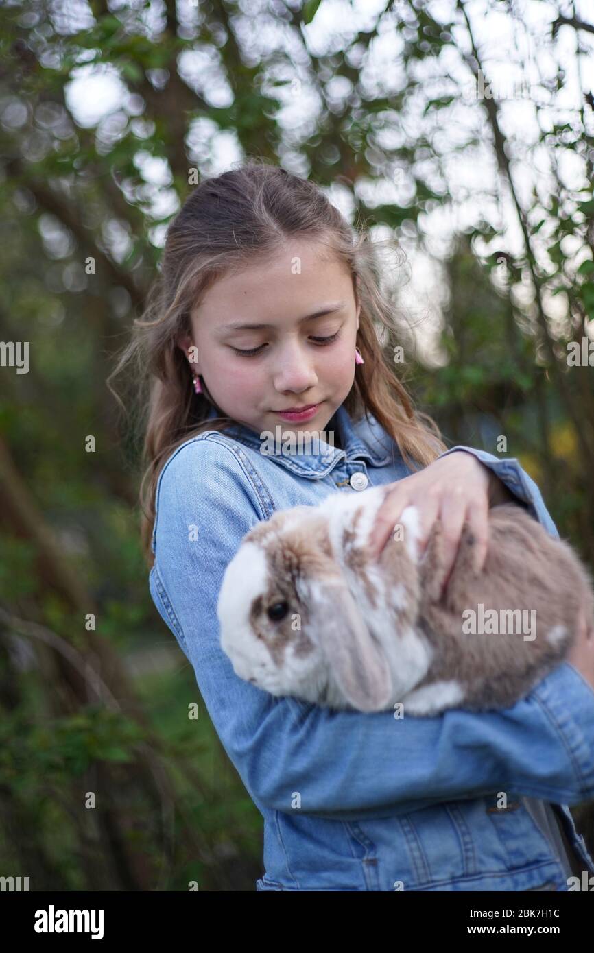 Portrait of a young blonde girl holding gently a pet bunny, rabbit in ...