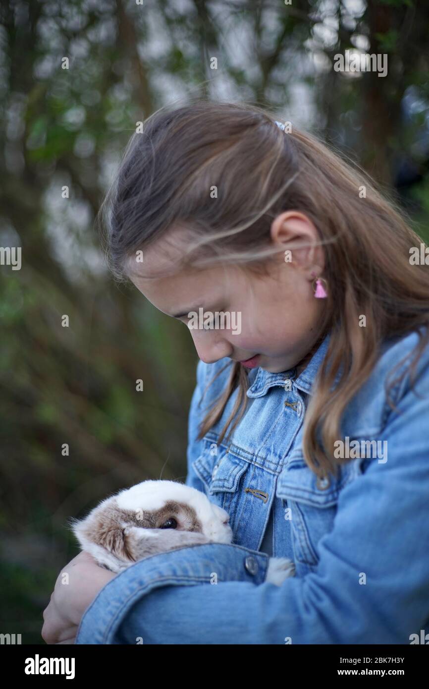 Portrait of a young blonde girl holding gently a pet bunny, rabbit in ...