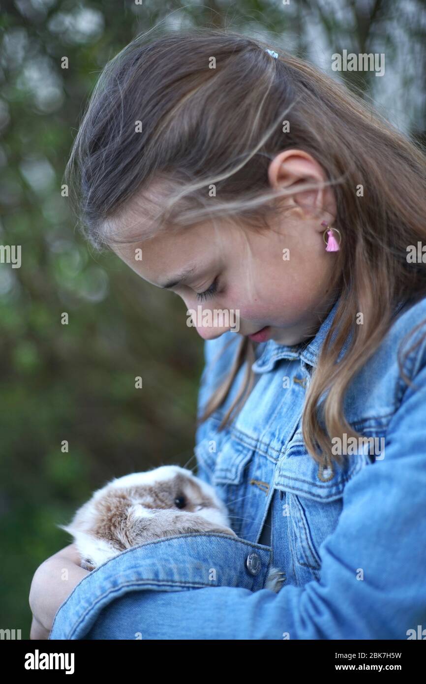 Portrait of a young blonde girl holding gently a pet bunny, rabbit in ...