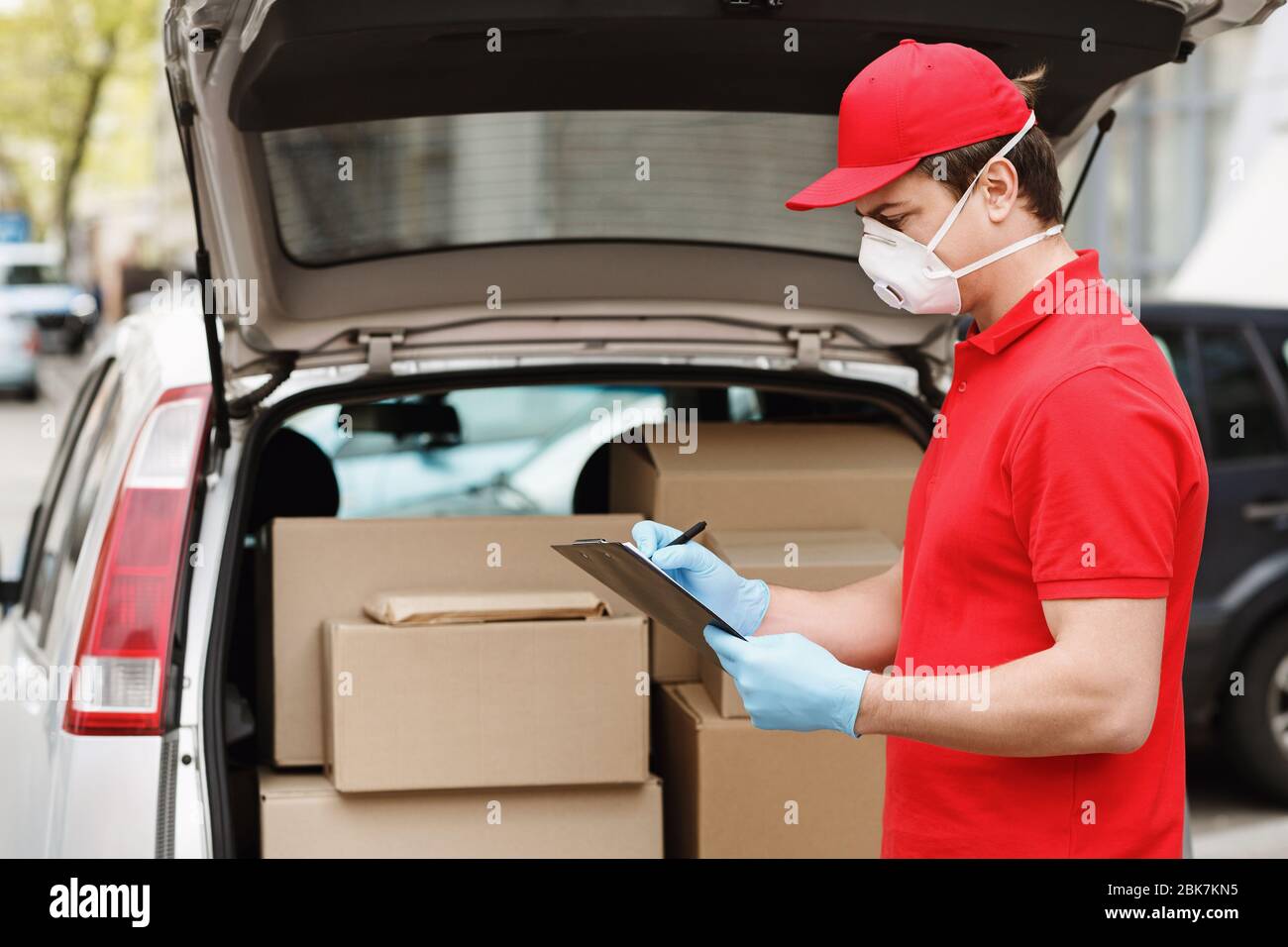 Delivery man near car with open trunk with parcels Stock Photo - Alamy