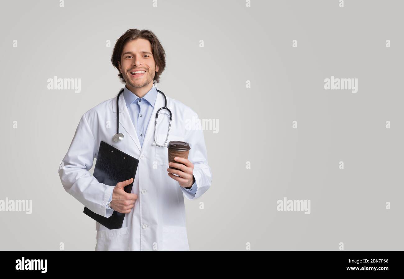 Portrait of young smiling doctor holding medical chart and takeout ...