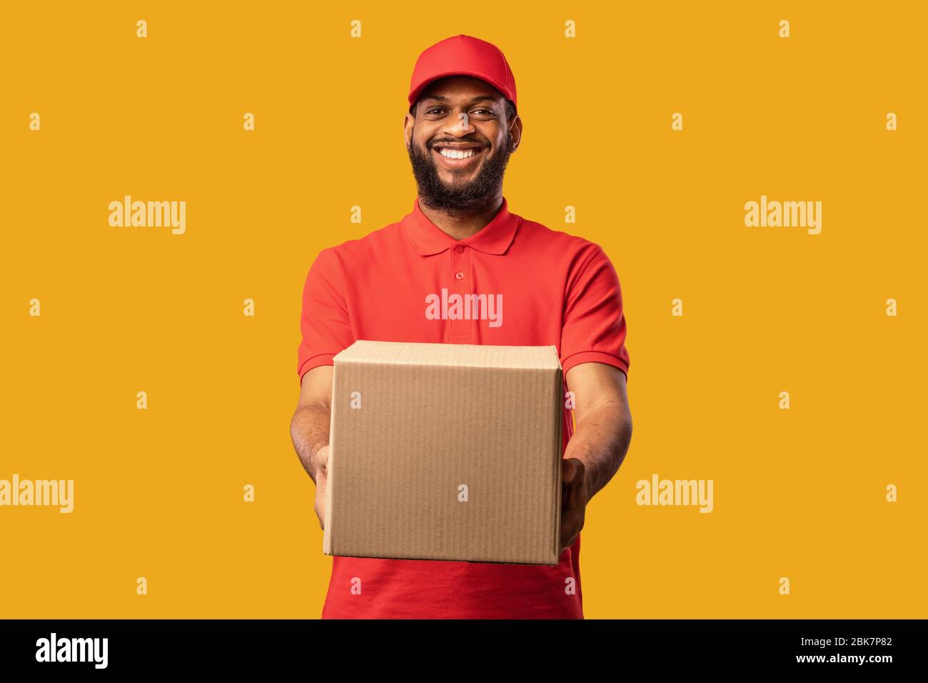 African Courier Offering Cardboard Box To Camera Over Yellow Background ...
