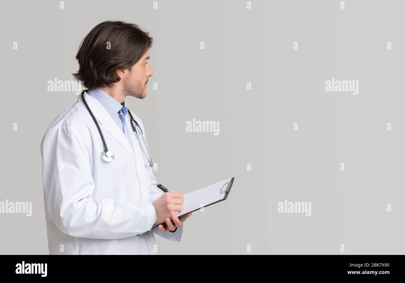 Confident doctor writing notes on clipboard and looking at copy space ...