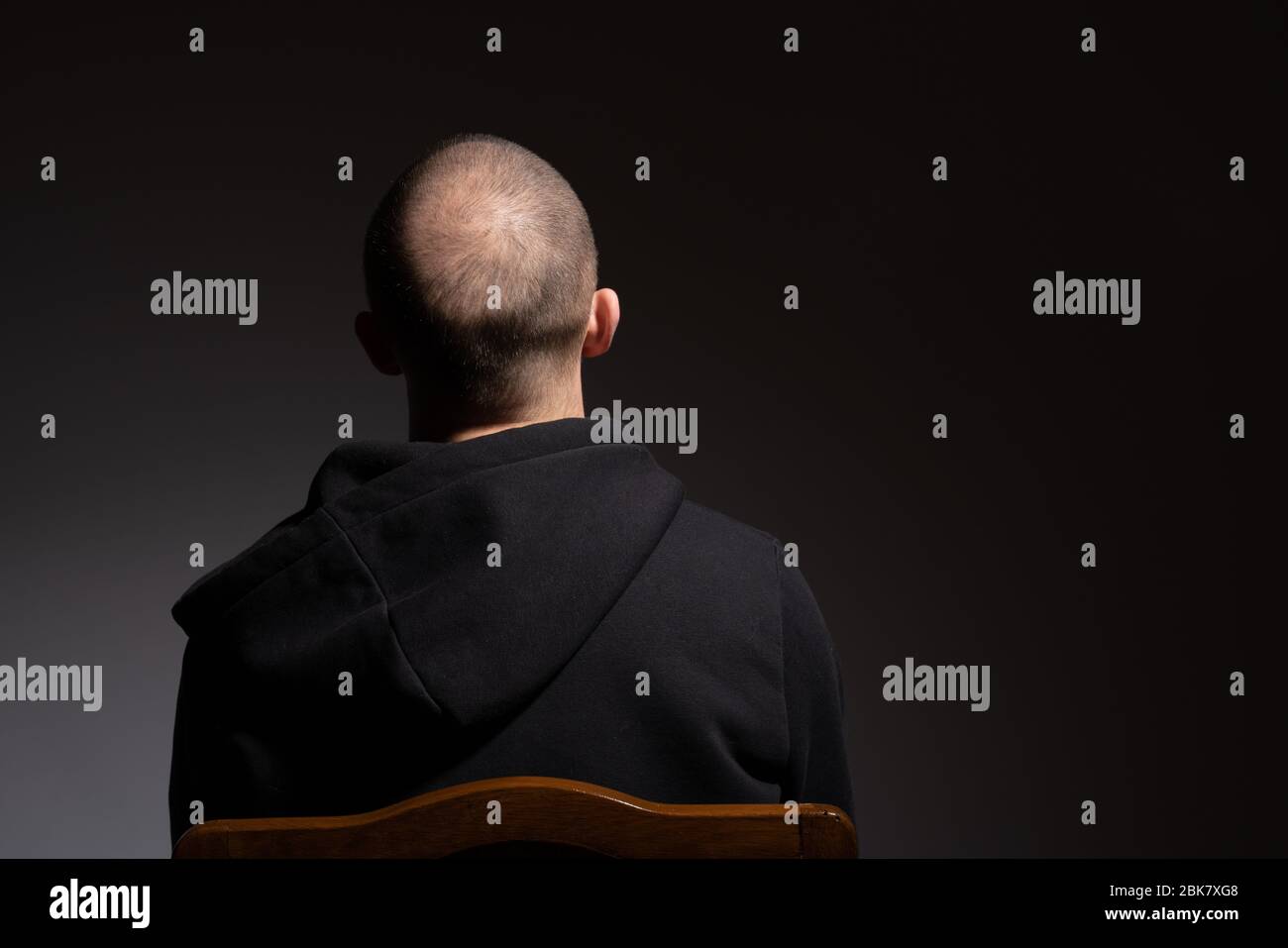 Back view of casual bald young man in black hoodie isolated on dark ...