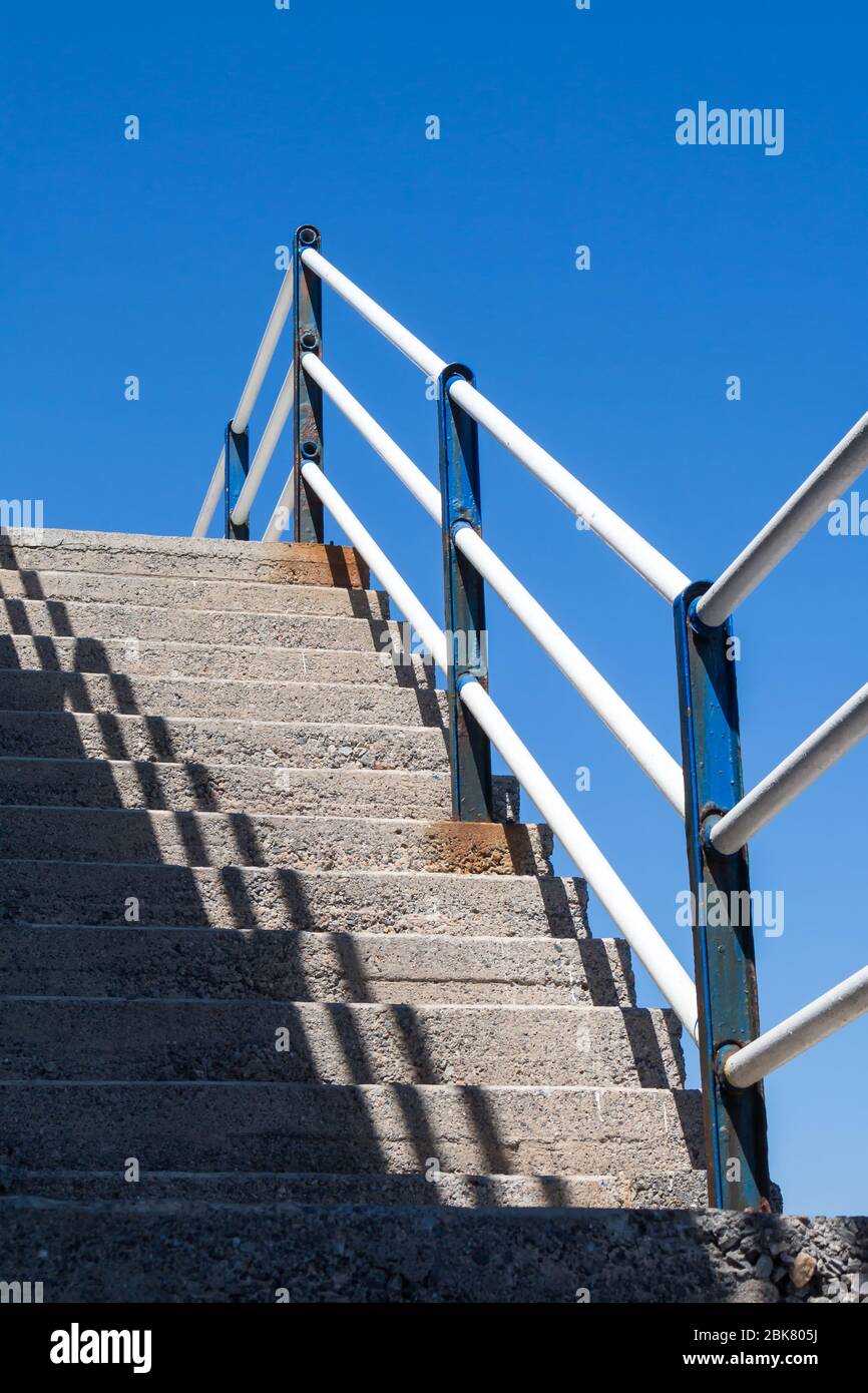 Simple concrete staircase outdoors with a diagonal shadow and a metal ...