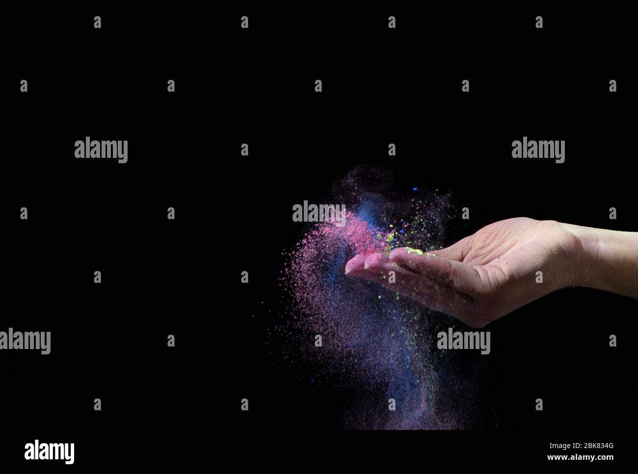 Colored powder exploding from palm hand, creating cloud of colour dust ...