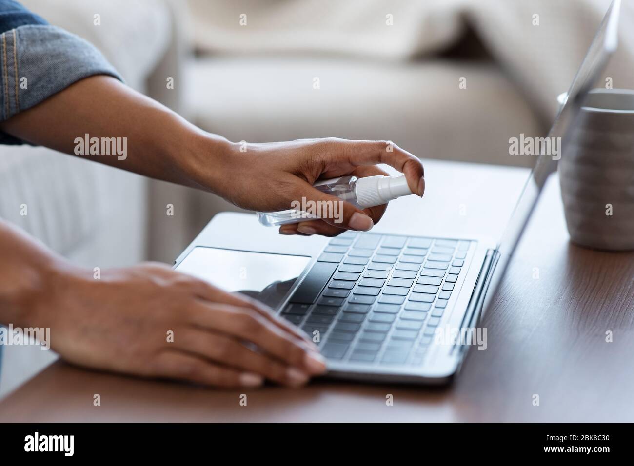 Unrecognizable black woman disinfecting laptop keyboard with antiseptic ...