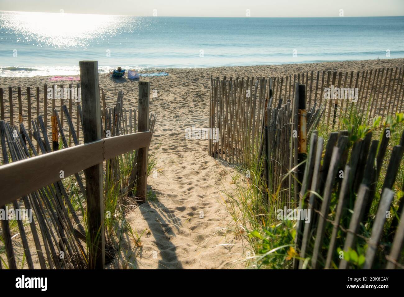 New England beach with wooden fence leading out to person sunbathing ...