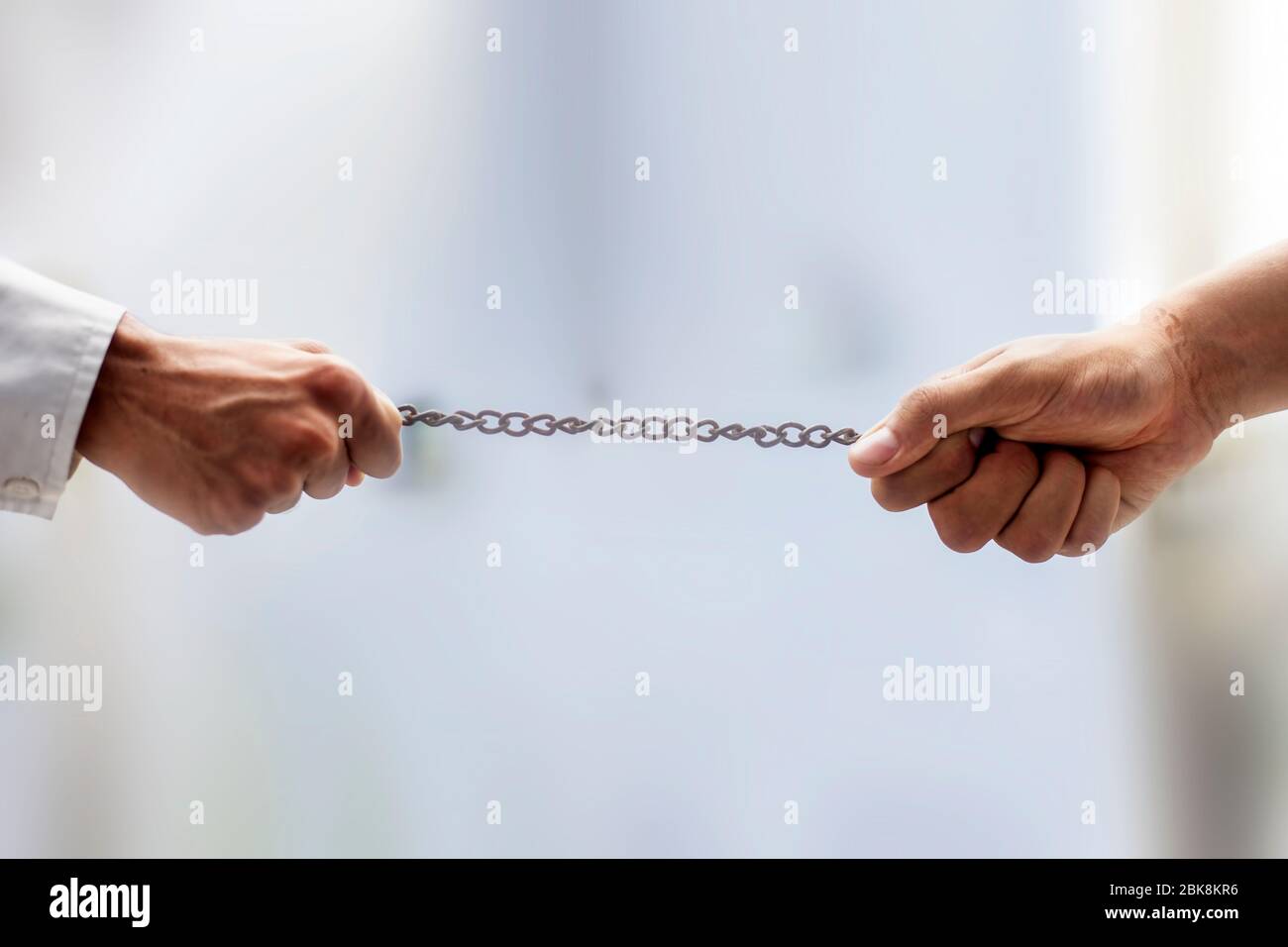 Shot of two hands on the end of a rusted metal chain pulling from both ...