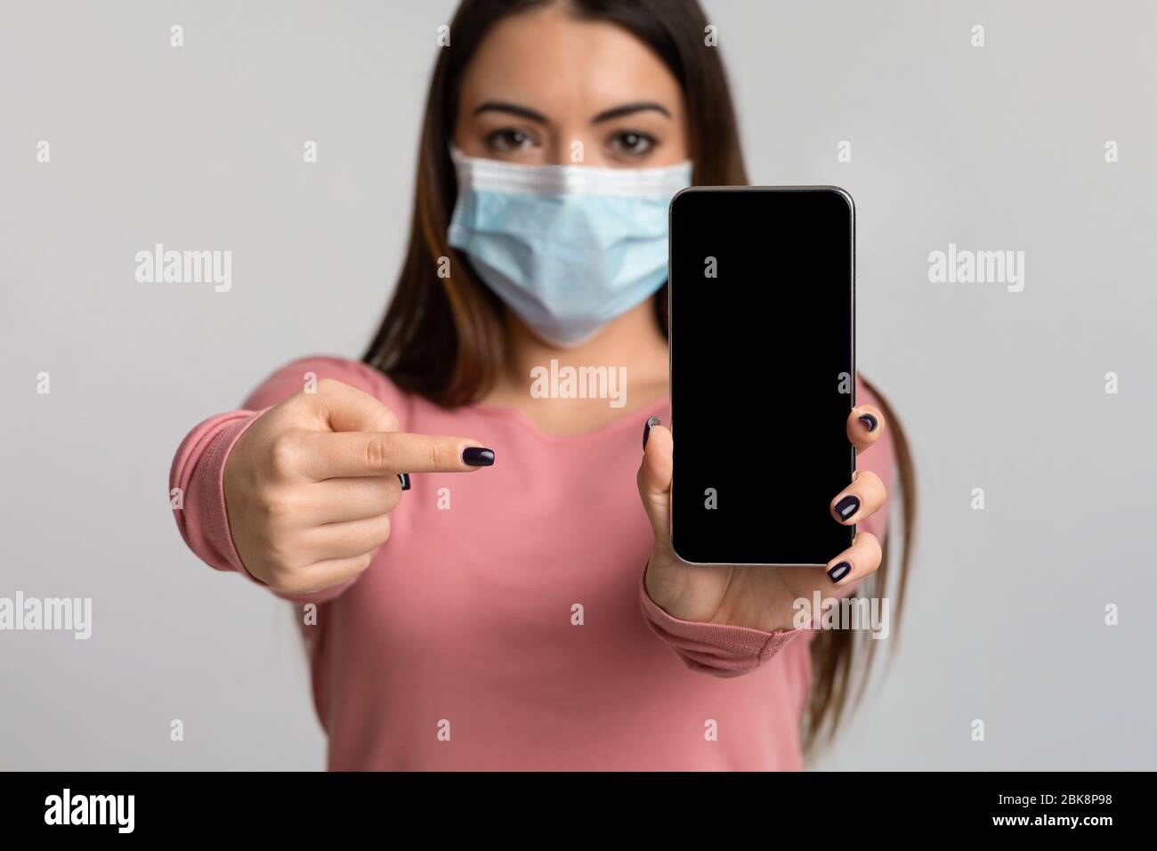 Young Woman In Medical Mask Pointing At Smartphone With Black Screen ...