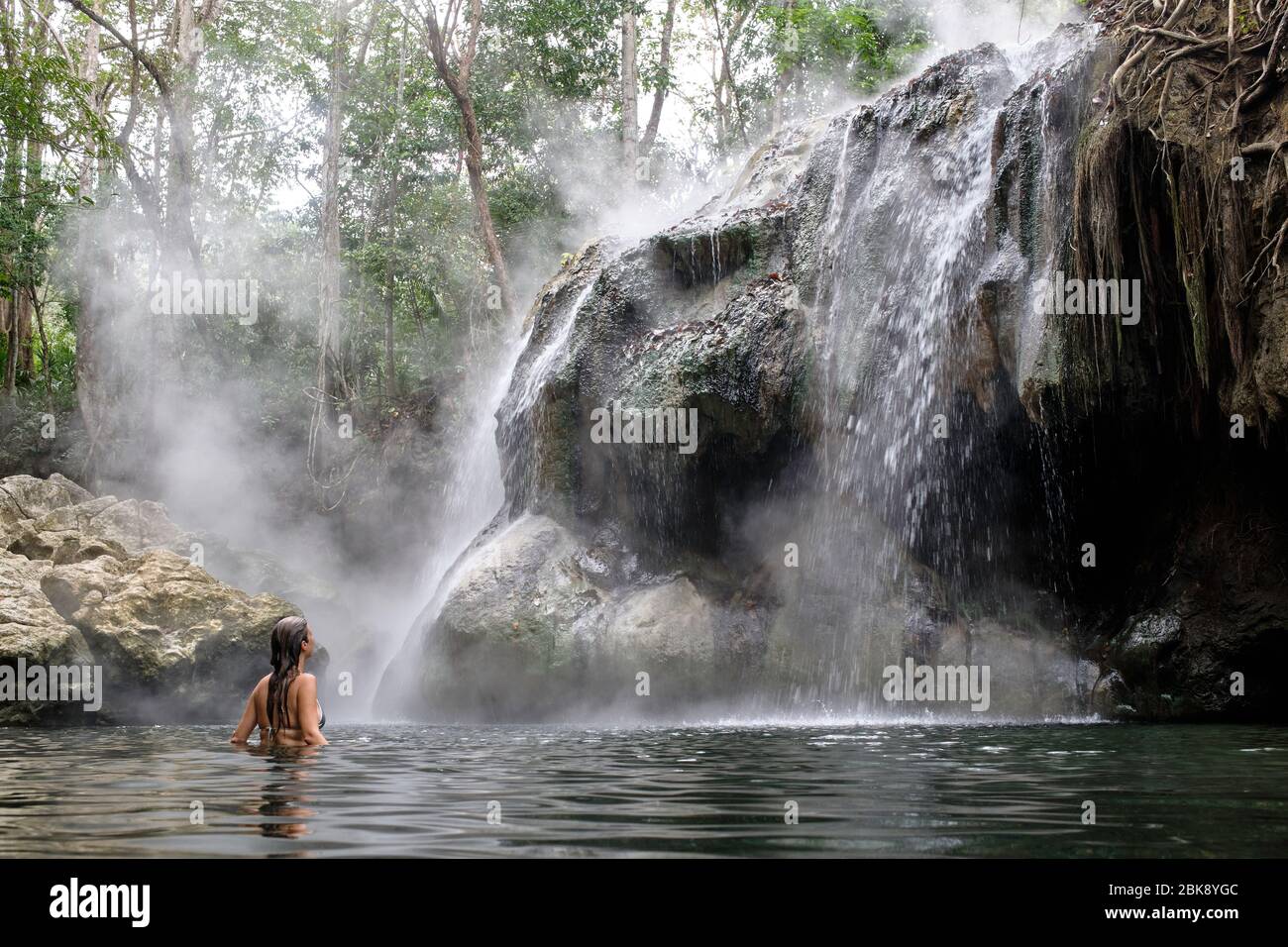 Woman in bikini taking a bath in a lake where a cascade of steaming hot ...