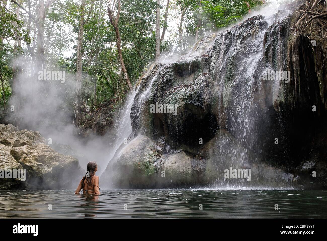 Woman in bikini taking a bath in a lake where a cascade of steaming hot ...