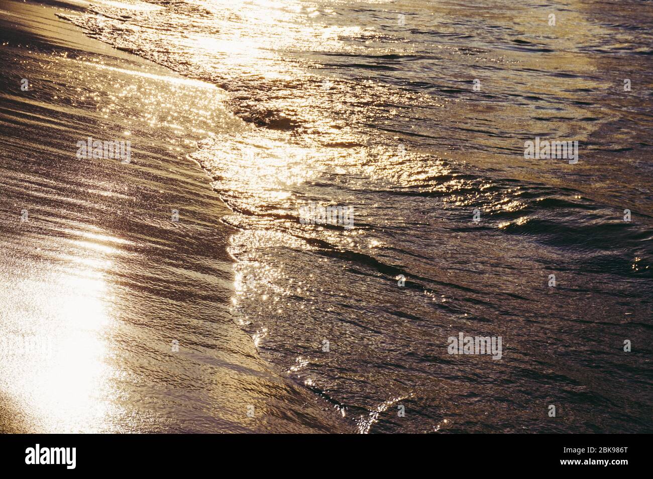 Sunset - sun reflecting in waves, shore Stock Photo - Alamy