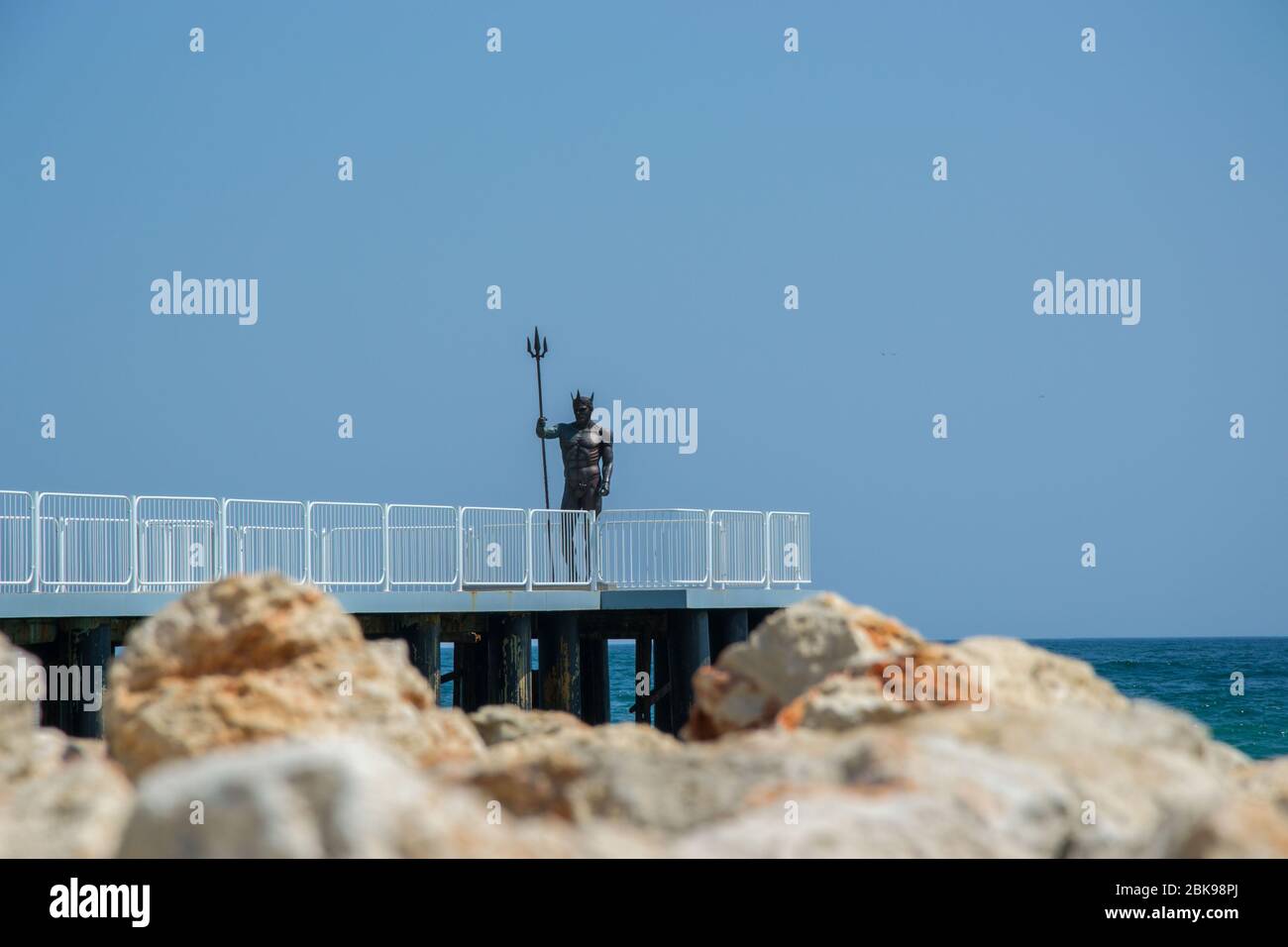 People walking on a pier with statue of Poseidon, bridge near the beach ...