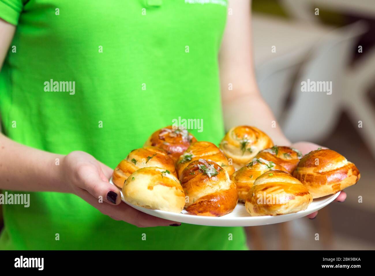 waitress in a green uniform holding a plate with fresh delicious buns ...