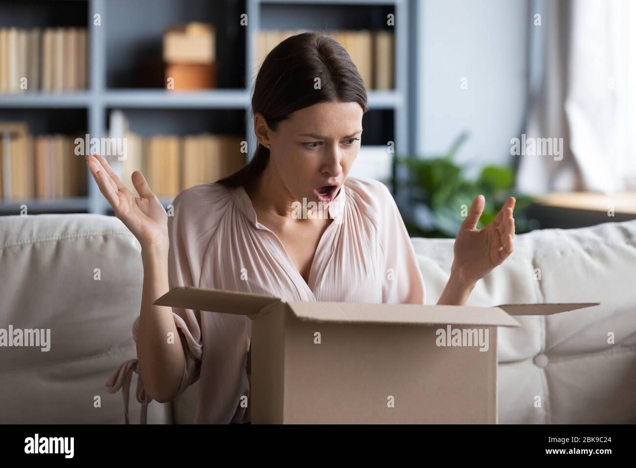 Angry shocked young woman unpacking parcel at home Stock Photo - Alamy