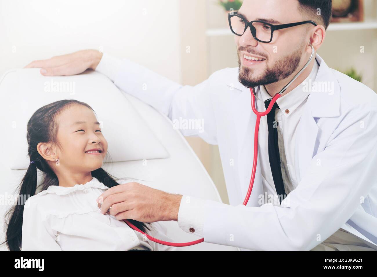 Young male doctor examining little kid in hospital office. The kid is ...