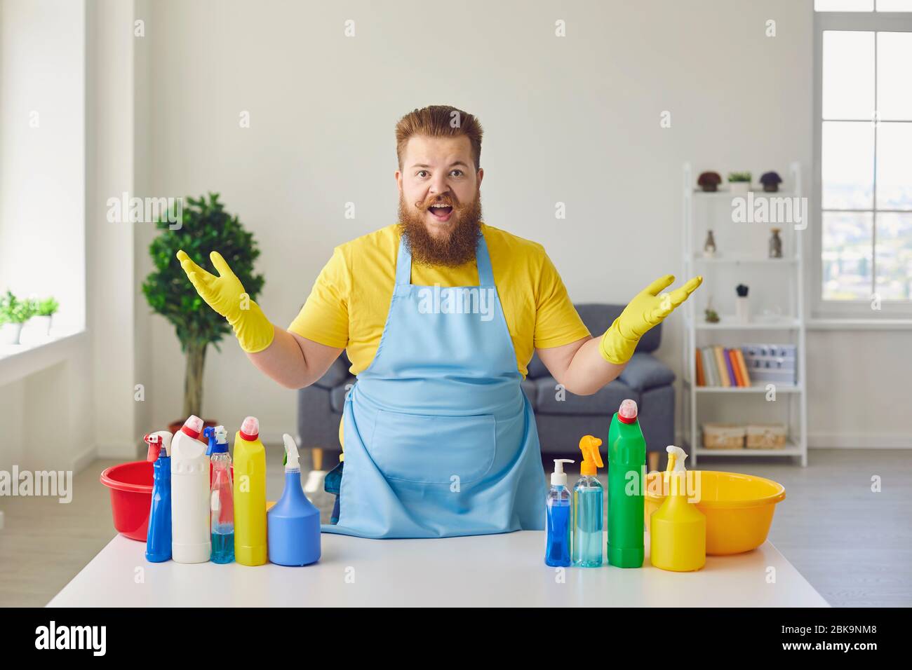 Funny fat man in an apron and yellow cleaning gloves is cleaning in the ...