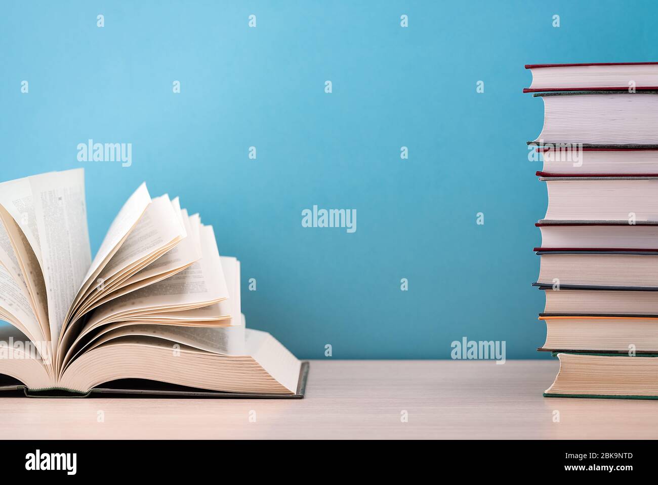 A large, thick hardcover book is lying on a light-wood table. The book ...