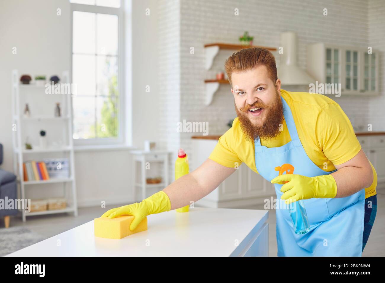 Funny fat man in an apron and yellow cleaning gloves is cleaning in the ...