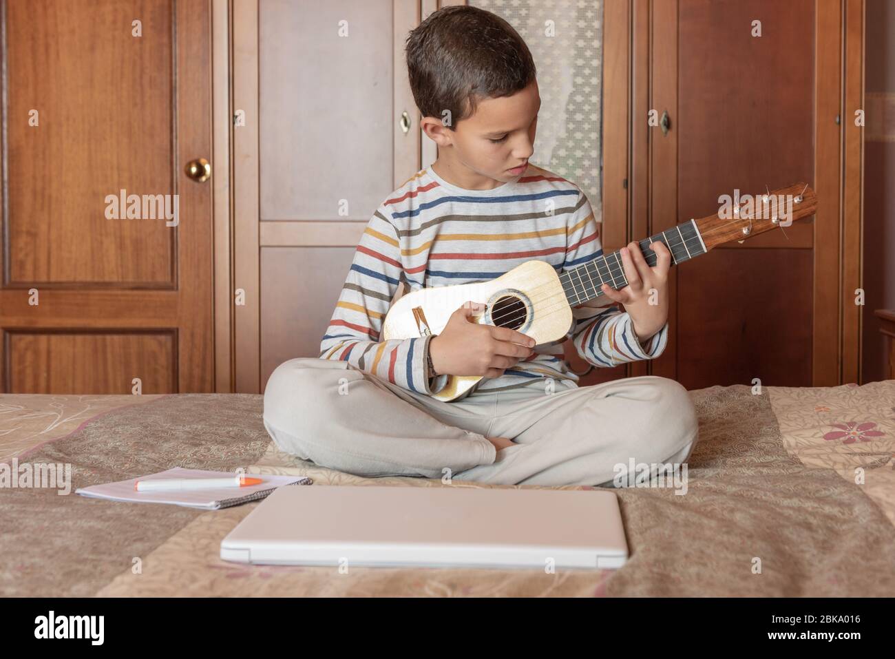 Front view of a little boy playing timple at home. The timple is a ...