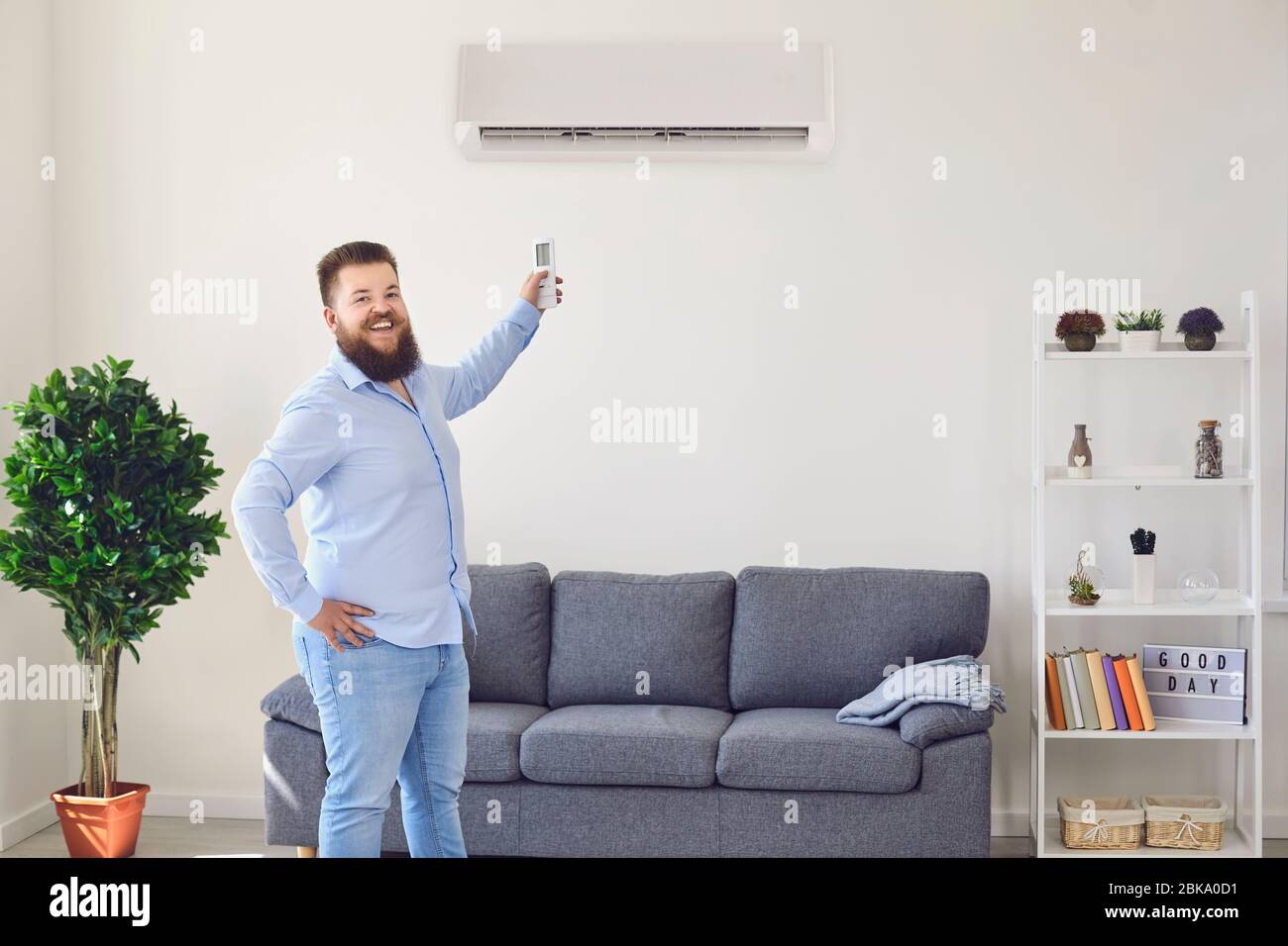 Fat funny man holding an air conditioning control panel at home. Air ...