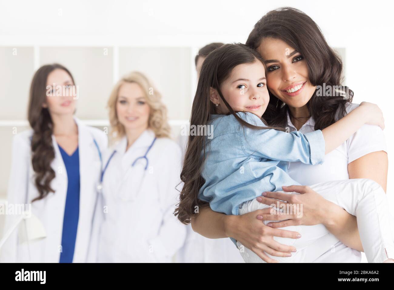 Mother And Daughter In Medical Clinic Team Of Doctors On Background