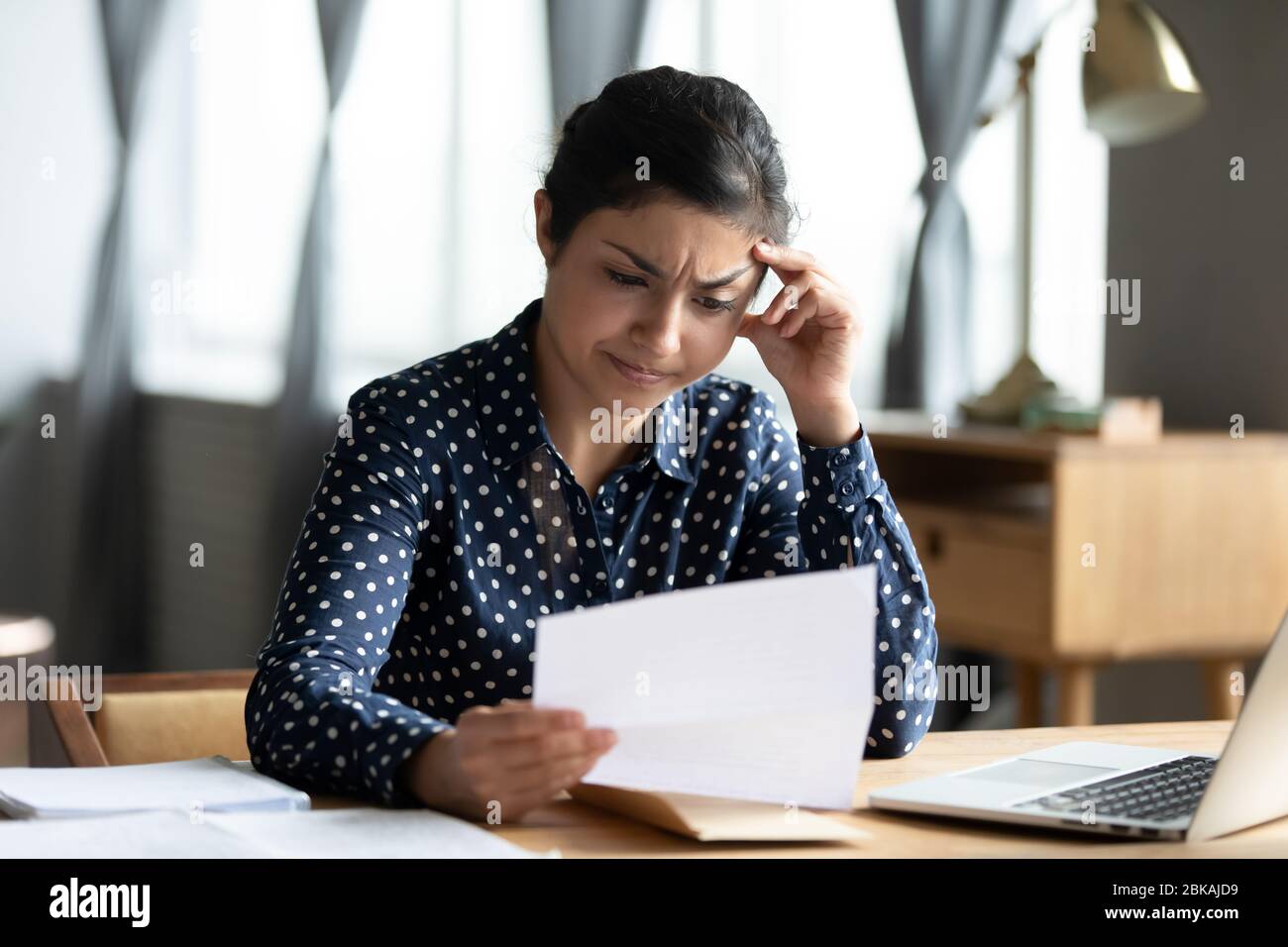 Stressed unhappy millennial indian girl looking through paper document ...