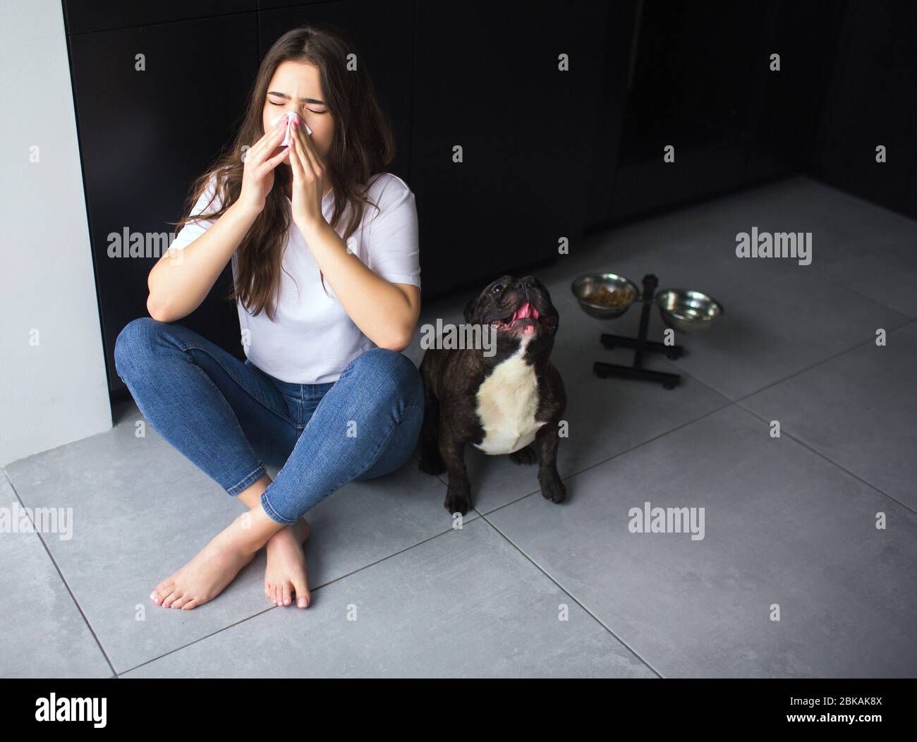 Young woman in kitchen during quarantine. Sit on floor and sneeze into ...