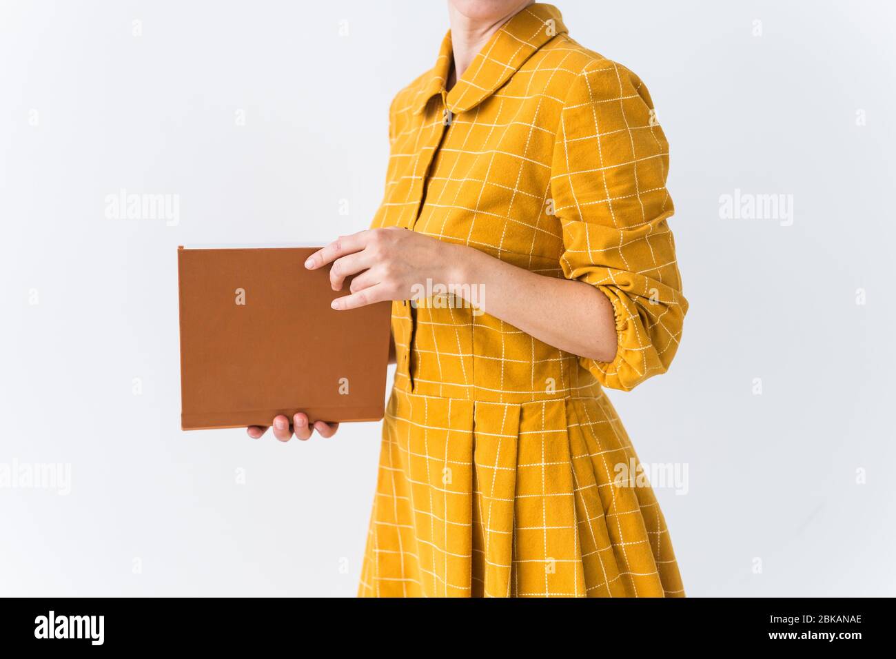 Close-up of girl in a yellow retro dress reading a book on white ...